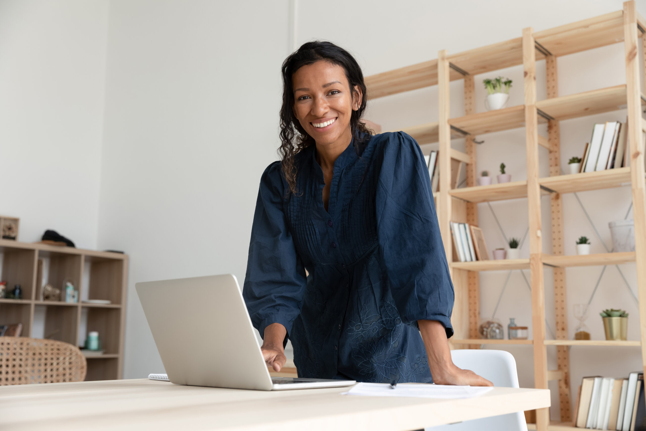 Smiling young biracial woman standing at table with computer. - Jo Garner